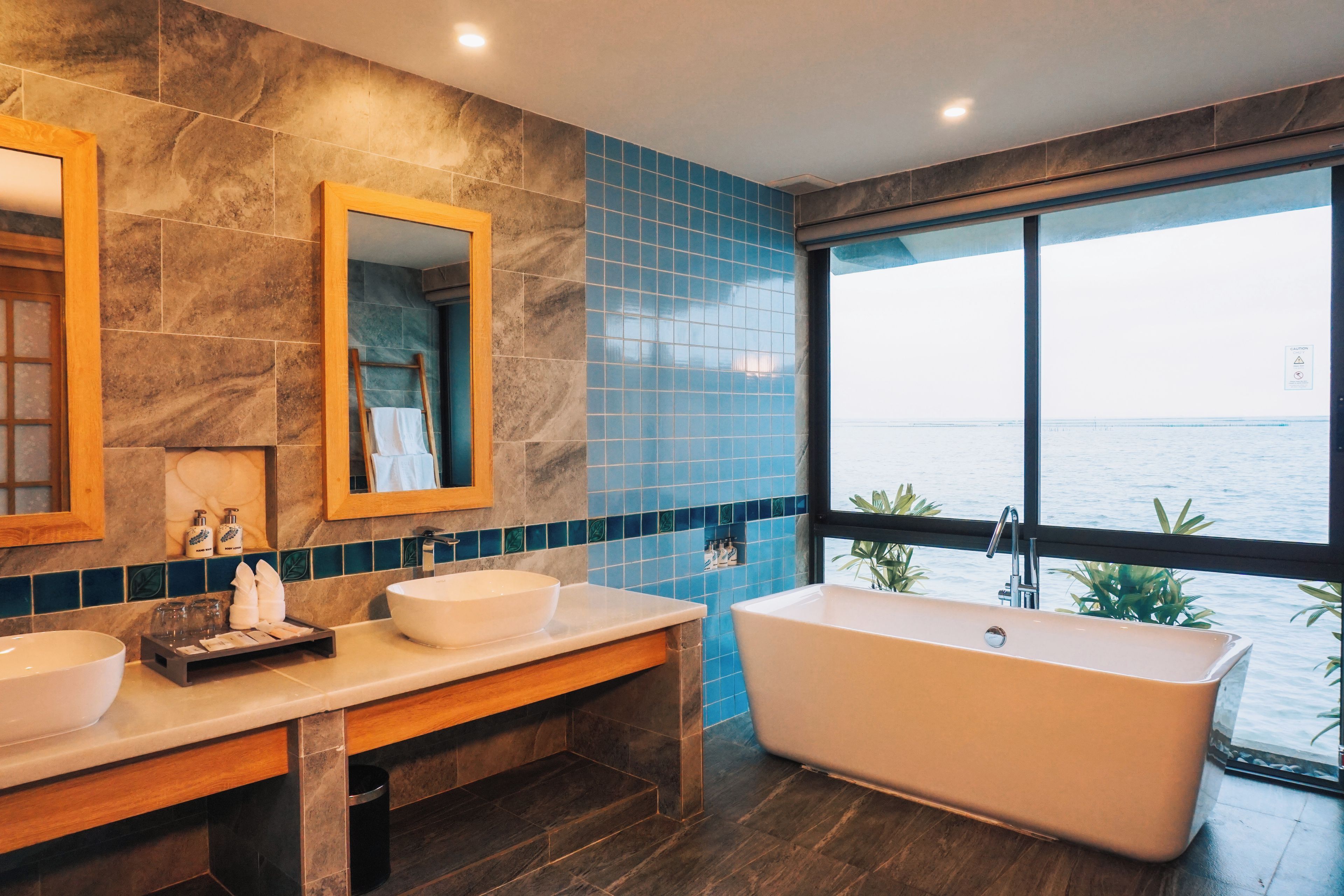 Uma casa de banho moderna com duas lavatórios, uma banheira grande e vista para o mar através de uma janela ampla.