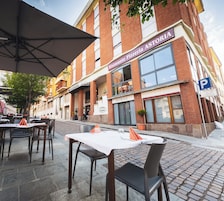 Uma área de refeições ao ar livre com mesas e cadeiras, um espaço coberto para sentar e um edifício com a placa 'Ristorante Astoria'.