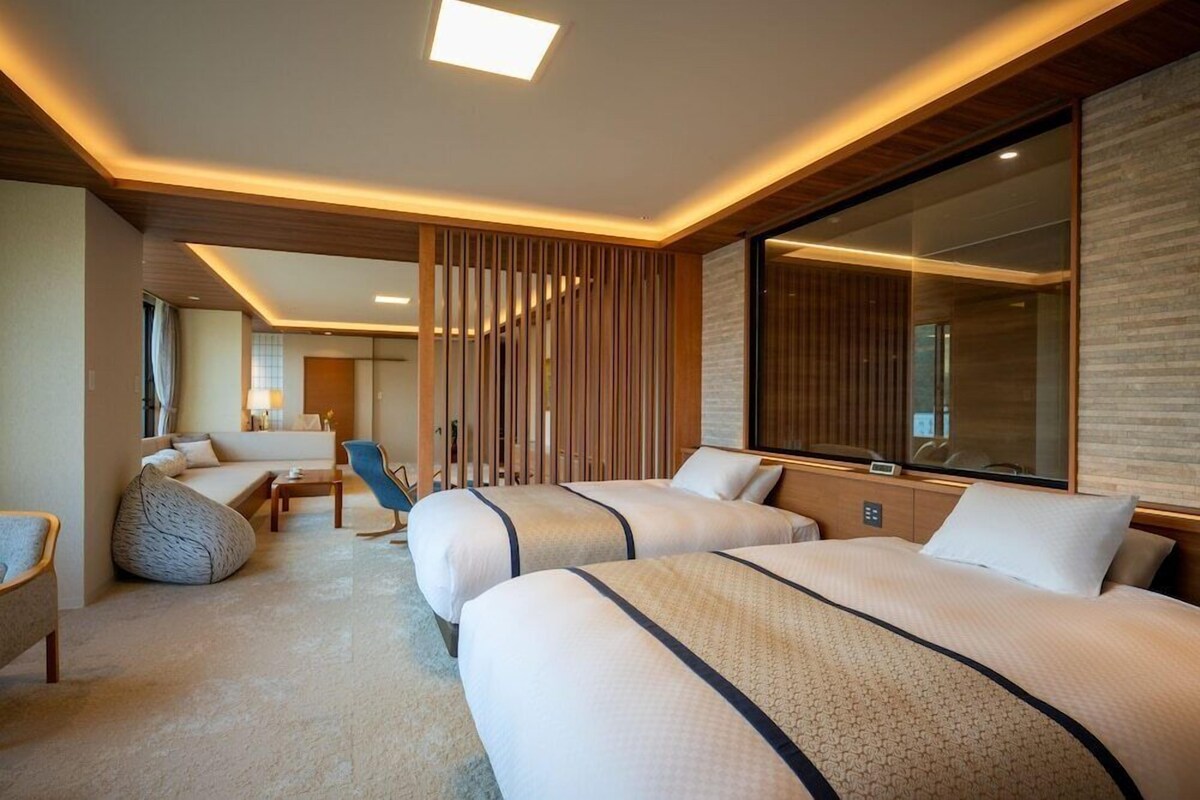 Quarto de hotel com duas camas, um sofá, uma cadeira e um espelho grande.