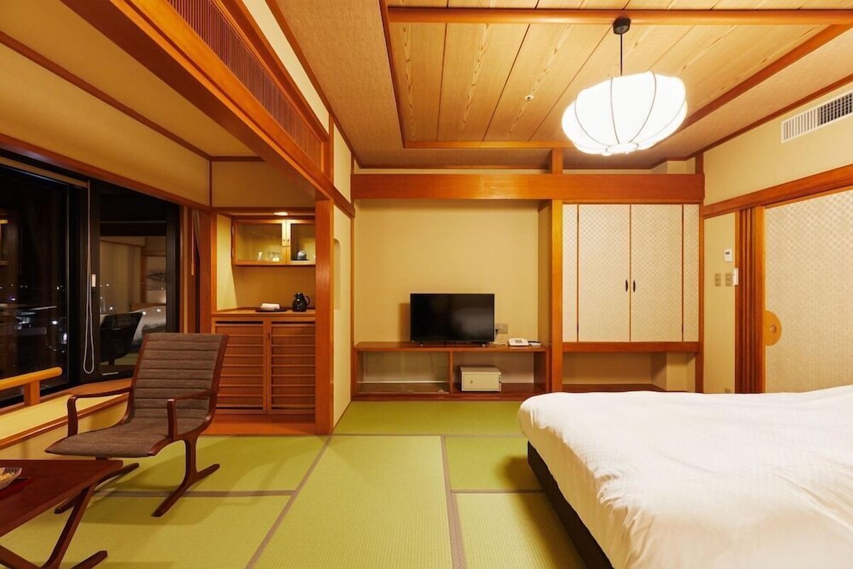 Quarto de hotel em estilo japonês tradicional, com tatames, televisão, cama e porta de correr.
