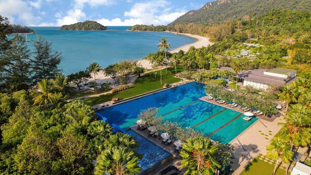 Um resort com uma grande piscina, uma praia e montanhas ao fundo.