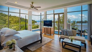 Um quarto espaçoso com uma cama grande, televisão e varanda com vista para a água.