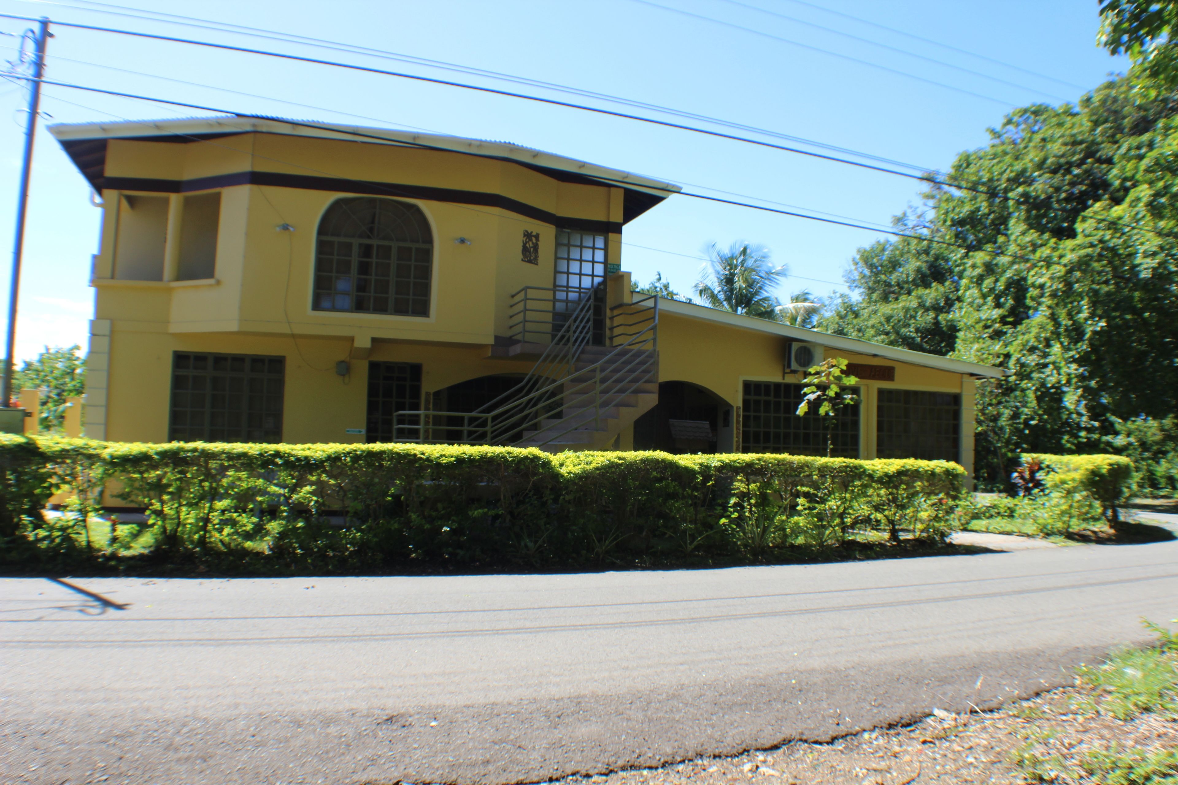Um edifício de dois andares com fachada amarela, janelas amplas e escadaria que leva ao andar superior.