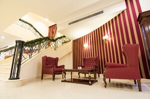 Um hall com escada, cadeiras estofadas em vermelho, mesa de centro de madeira e parede listrada.