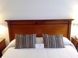 Uma cama bem arrumada com cabeceira de madeira, duas almofadas listradas e lençol branco.