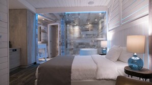 Quarto de hotel moderno com uma cama grande, banheiro com paredes de vidro e vista para a cidade.