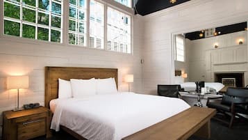 Quarto de hotel com uma cama grande, mesa de cabeceira de madeira, escrivaninha, cadeira e lareira.