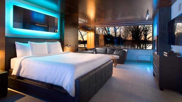 Quarto moderno com uma cama grande, área de estar e vista para o exterior.