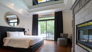 Quarto de hotel moderno com uma cama grande, um espelho redondo, um espaço de estar e uma televisão na parede.