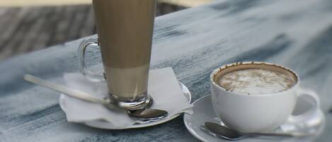 Uma mesa com um copo alto de café gelado e uma xícara de café em uma mesa de madeira ao ar livre.