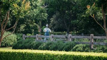Estátua de uma pessoa em um jardim com cerca de madeira e vegetação exuberante.