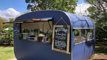 Um food truck azul com uma placa que diz 'BEM-VINDOS Hóspedes Inhouse' e uma placa para 'The Pool Bar', com garrafas e copos em exposição.