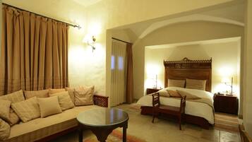 Quarto de hotel com sofá, cama, mesa de vidro redonda e duas mesas de cabeceira com luminárias.