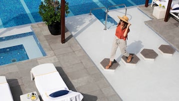 Área de piscina com espreguiçadeiras, uma planta em vaso e uma pessoa caminhando.
