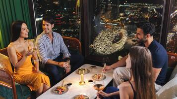 Um grupo de pessoas sentadas à mesa, com sushi e bebidas, apreciando a vista da cidade à noite.