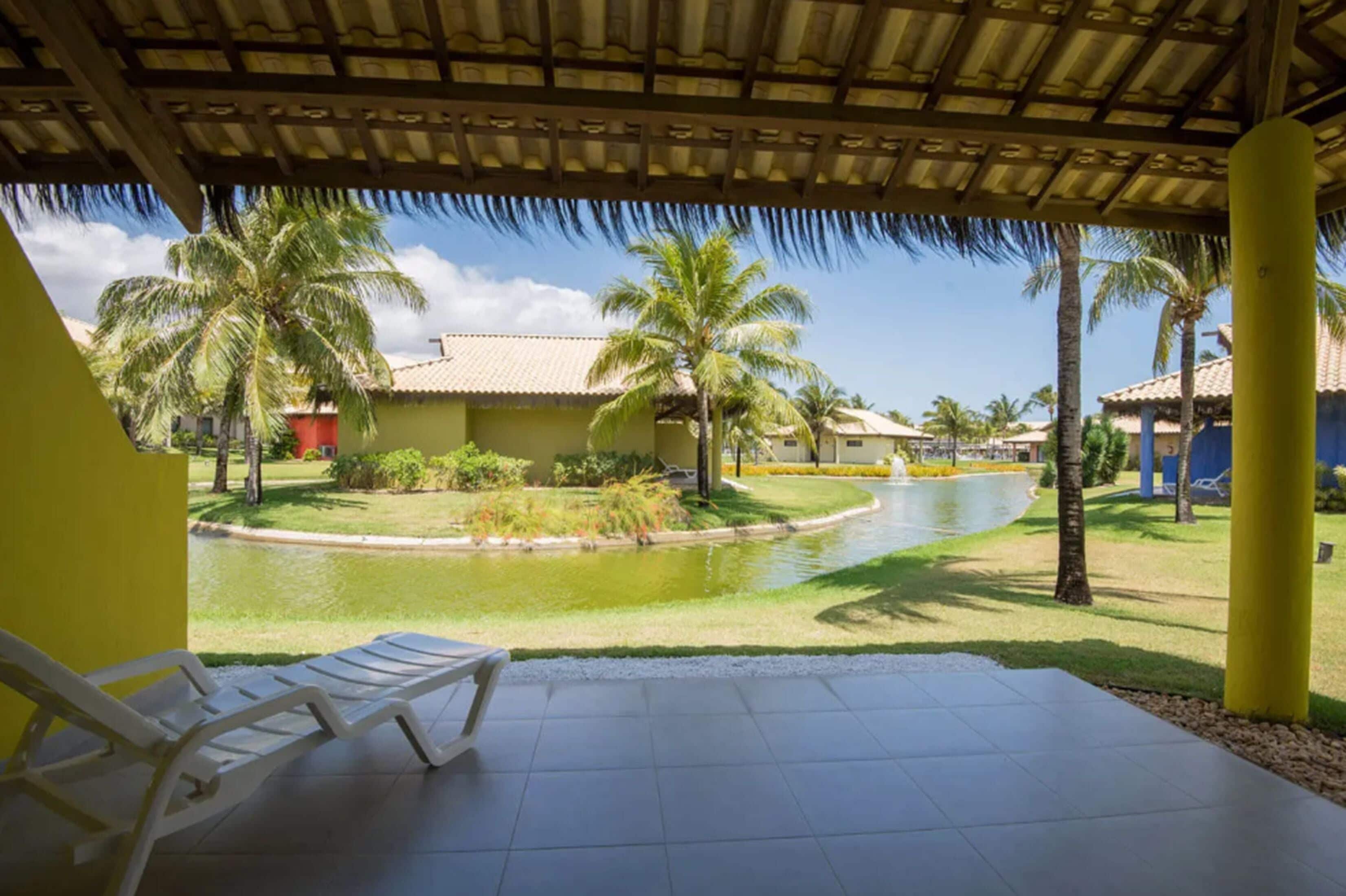 Uma área externa coberta com piscina, palmeiras e uma espreguiçadeira.
