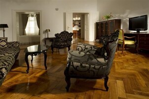 Uma sala de estar com sofá, duas poltronas, mesa de centro, televisão e um armário.