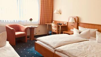 Quarto de hotel com cama, escrivaninha, cadeira e janela com cortinas.