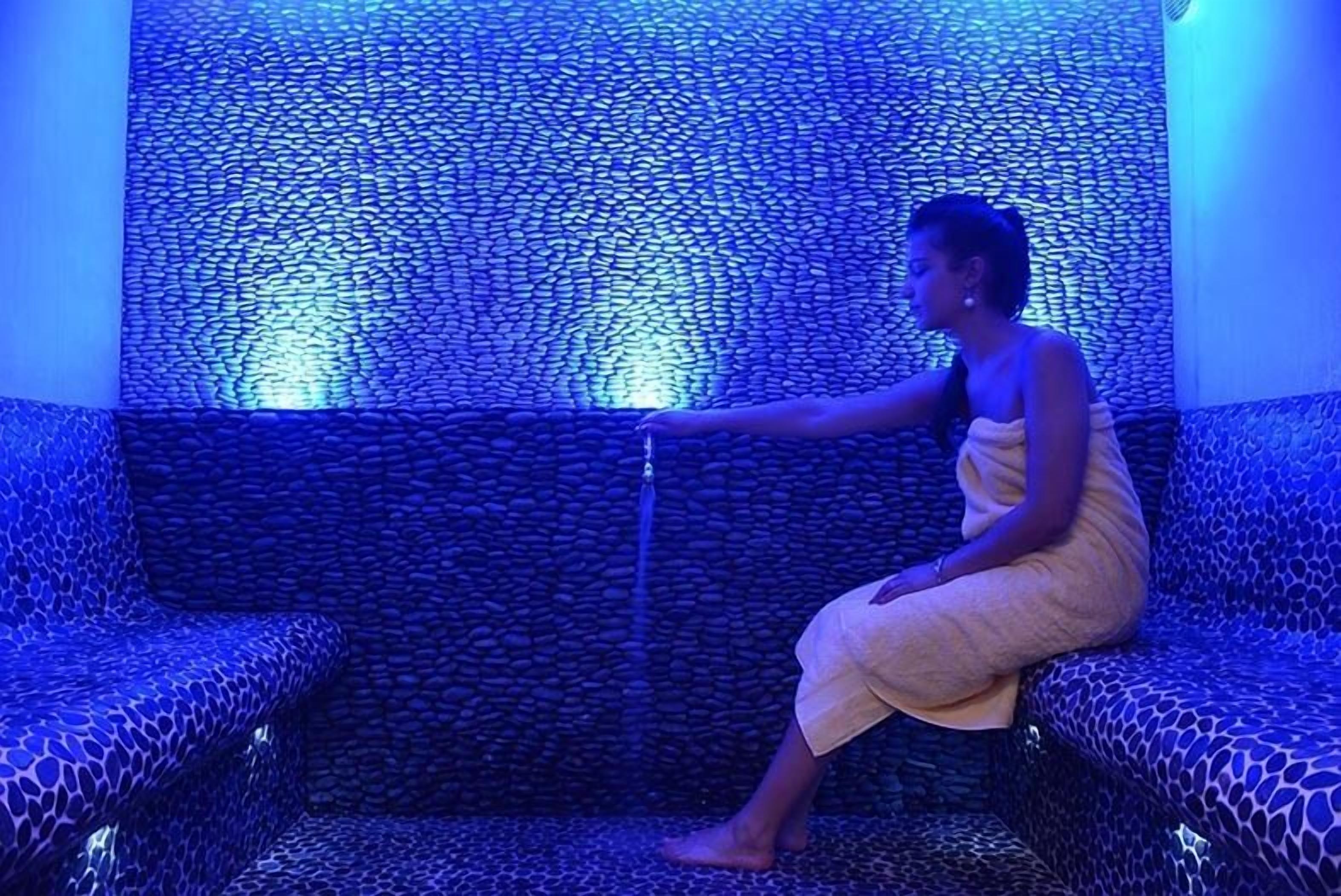 Uma pessoa sentada em um banco em um quarto com parede texturizada e iluminação azul.