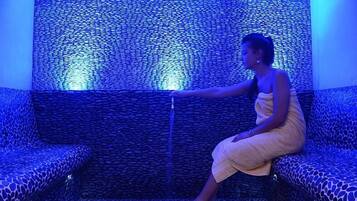 Uma pessoa sentada em um banco em um quarto com parede texturizada e iluminação azul.
