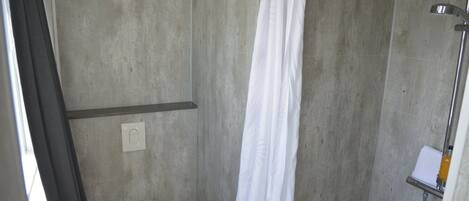 Um banheiro com vaso sanitário, chuveiro com cortina branca e porta-toalhas.