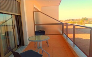 Varanda com mesa e cadeiras de vidro, vista para a paisagem e porta de correr de vidro.