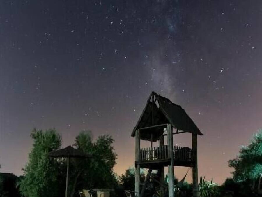 Estrutura de madeira rústica com varanda, localizada próxima a uma piscina calma que reflete o céu noturno.