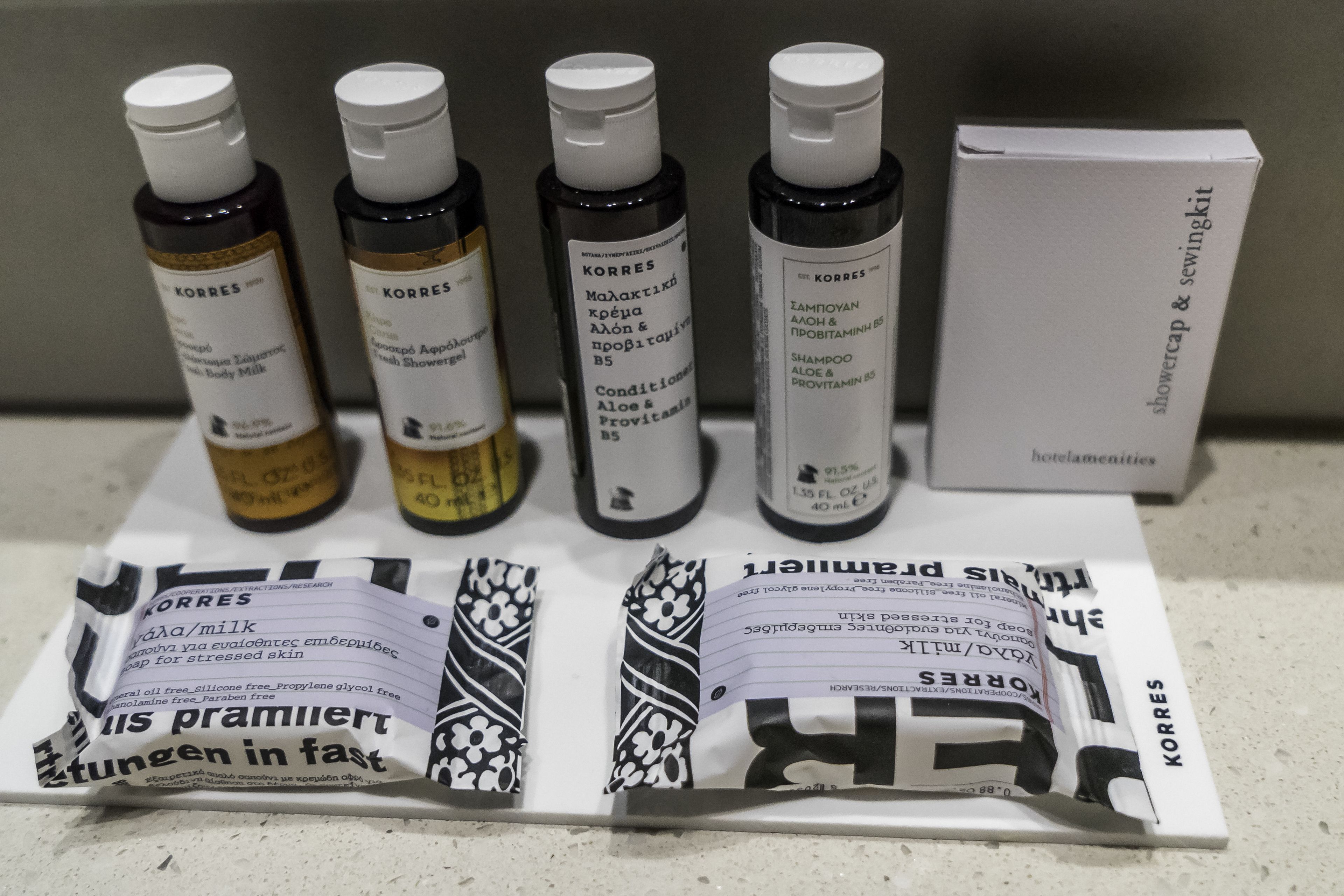Quatro frascos de produtos Korres e uma caixa com touca de banho e kit de costura Korres sobre uma mesa.