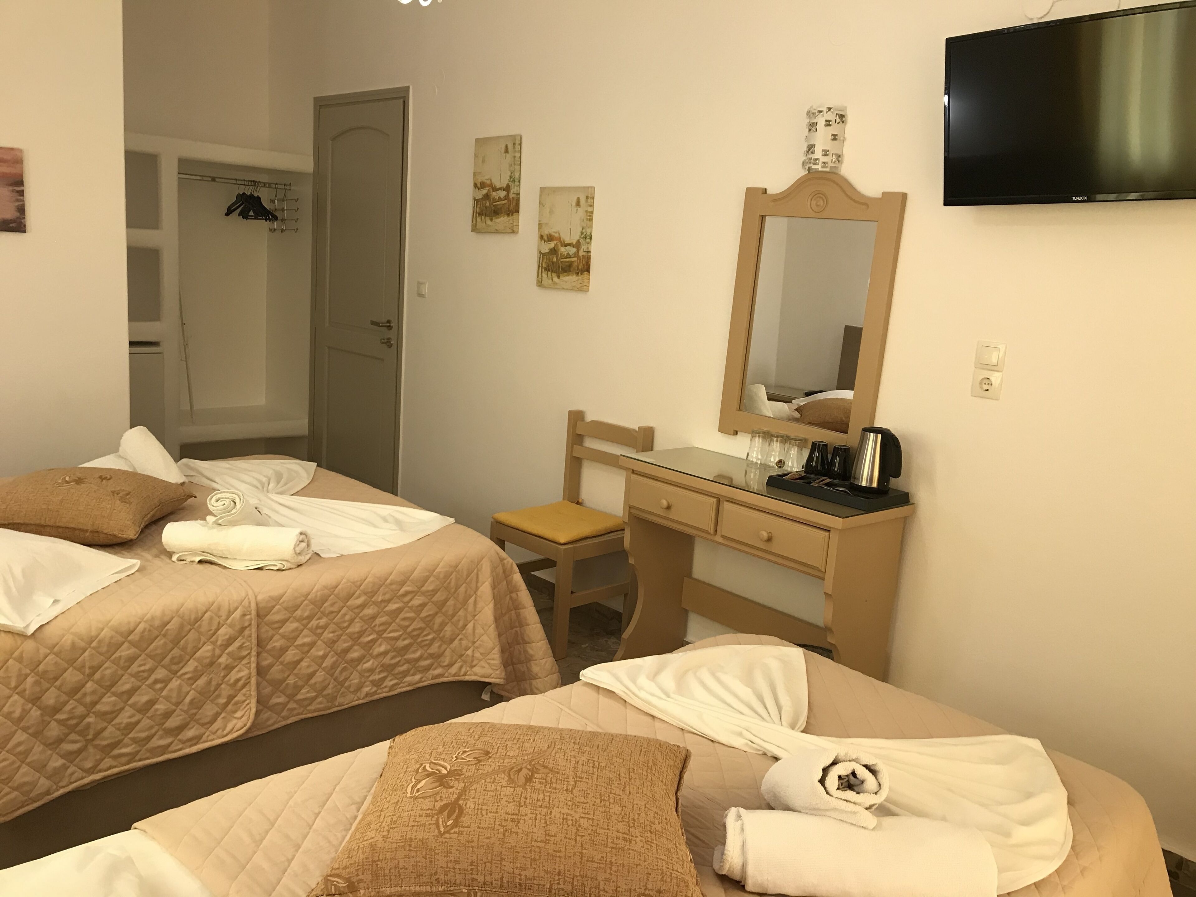 Quarto de hotel com duas camas, uma escrivaninha, uma cadeira, uma televisão e um espelho.