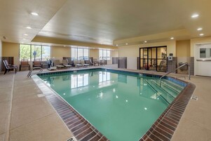 Piscina interior com água cristalina, cercada por espreguiçadeiras e área de sol.