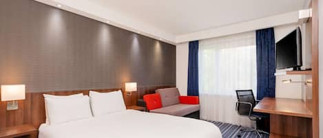 Quarto de hotel com uma cama grande, uma escrivaninha com cadeira, televisão e janela com cortinas.