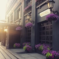 Fachada de hotel com cestos de flores pendurados e uma placa com a inscrição 'HOTEL'.