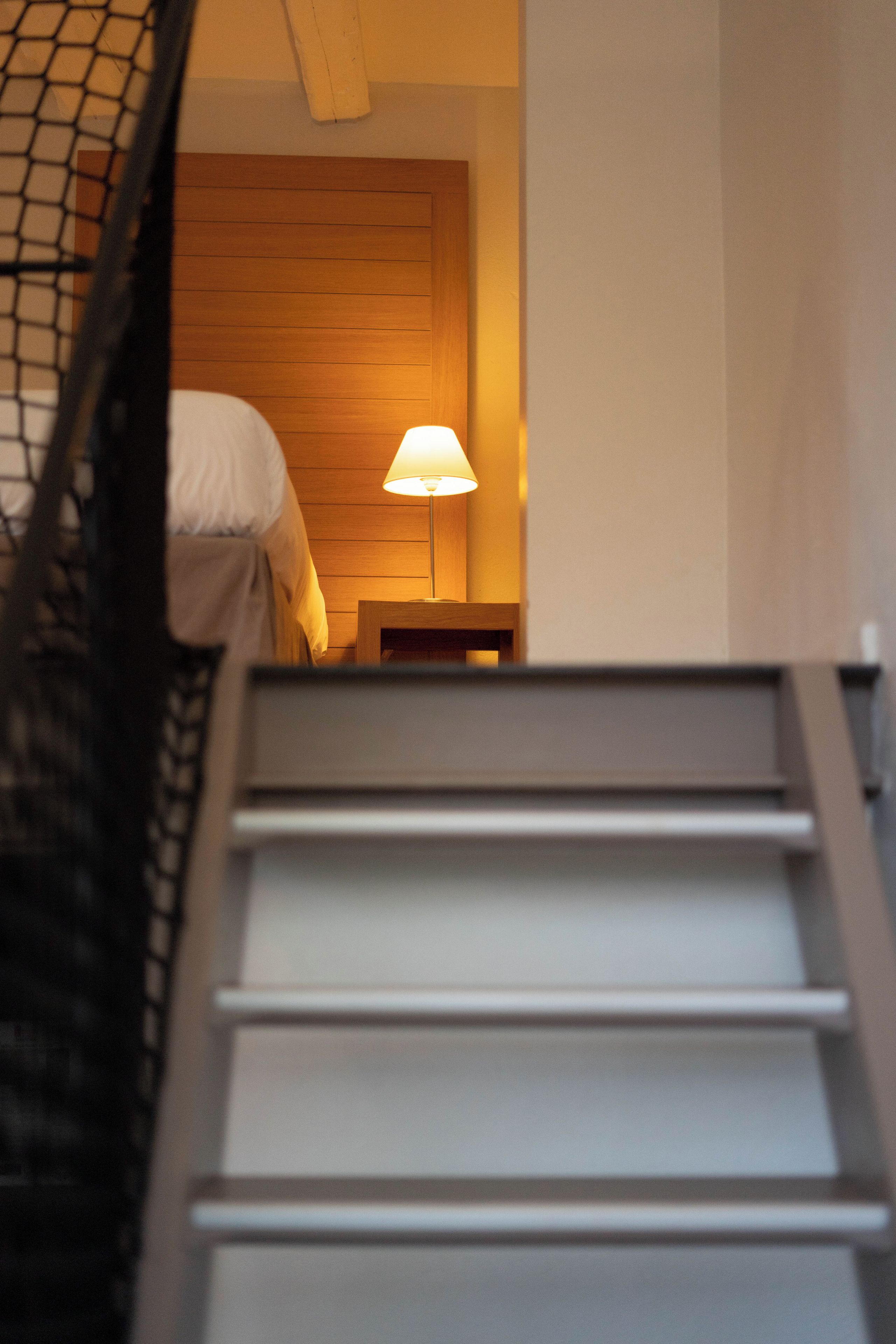 Escada que leva a um quarto com porta de madeira e luminária de cabeceira.