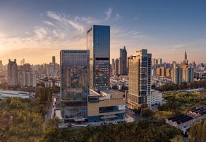 Um hotel moderno com fachada de vidro, rodeado por um horizonte urbano denso.