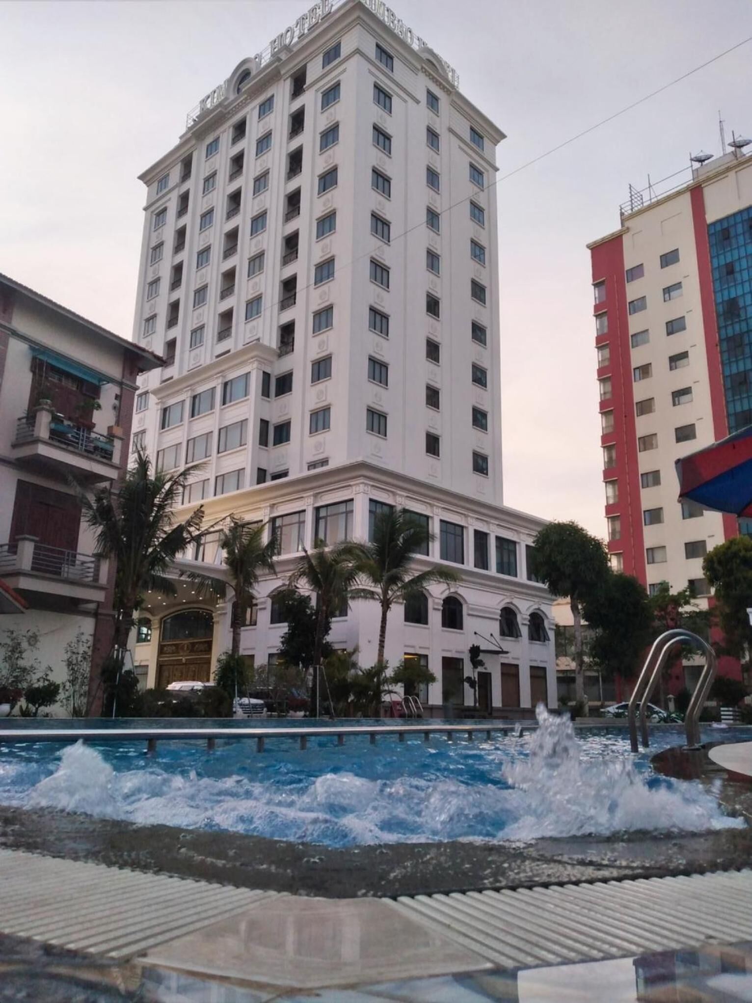 Um hotel com grande área de piscina, palmeiras e um edifício moderno com vários andares.
