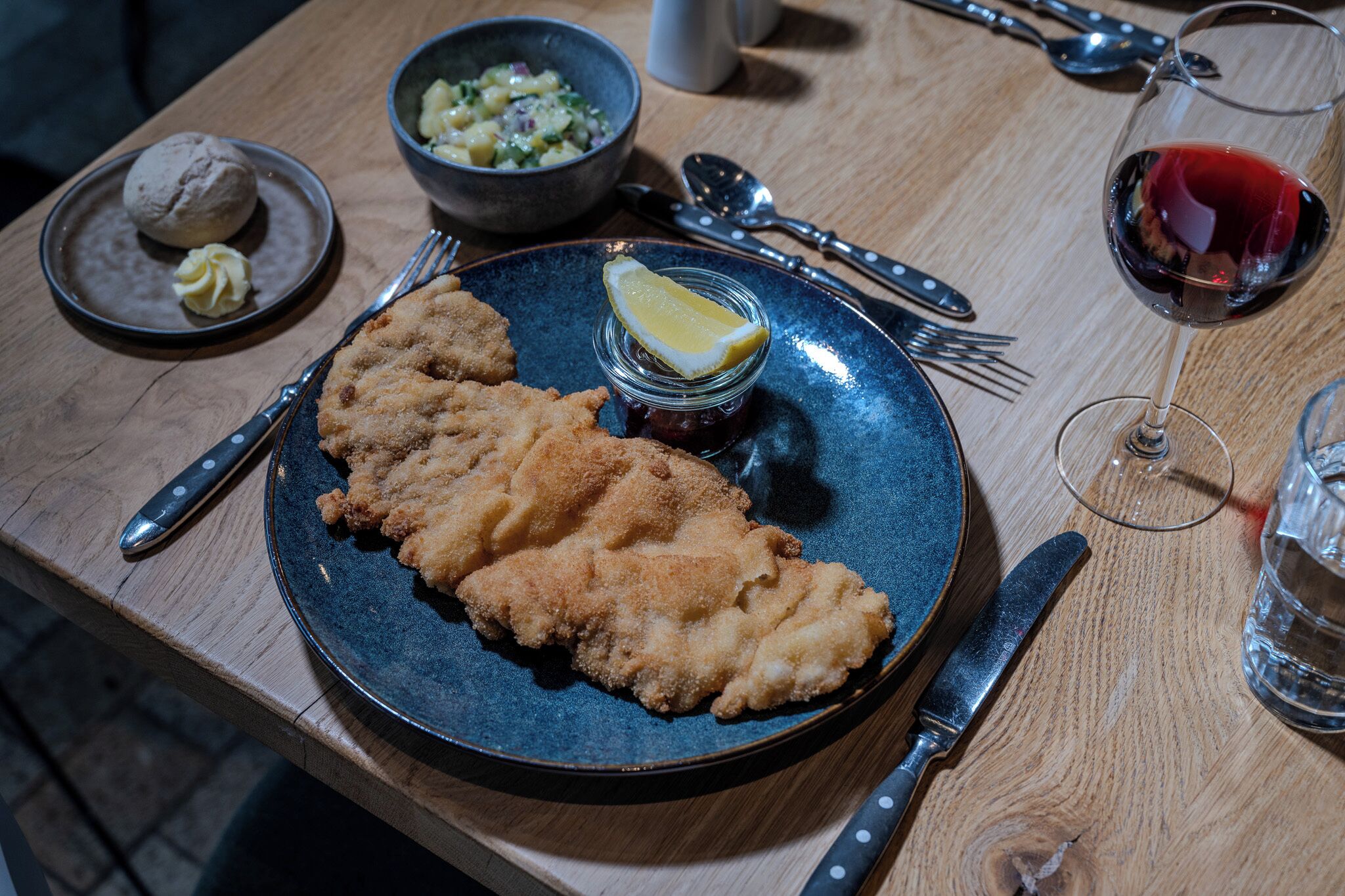 Um prato com escalope à milanesa, um pedaço de limão e um pequeno pote de molho sobre um prato azul.