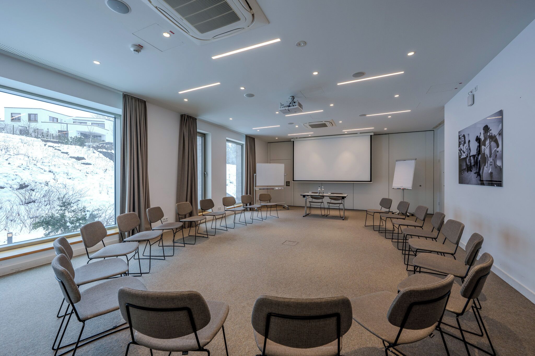 Sala de conferências com uma tela grande, projetor e assentos dispostos em semicírculo.