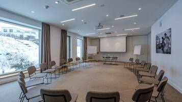 Sala de conferências com uma tela grande, projetor e assentos dispostos em semicírculo.