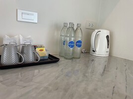 Uma bancada de cozinha com uma chaleira, duas garrafas de água, um suporte com canecas e um recipiente com sachês de chá Lipton, e uma tomada.