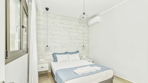 Quarto com cama, mesa de cabeceira, janela com cortinas e luminária pendente geométrica.