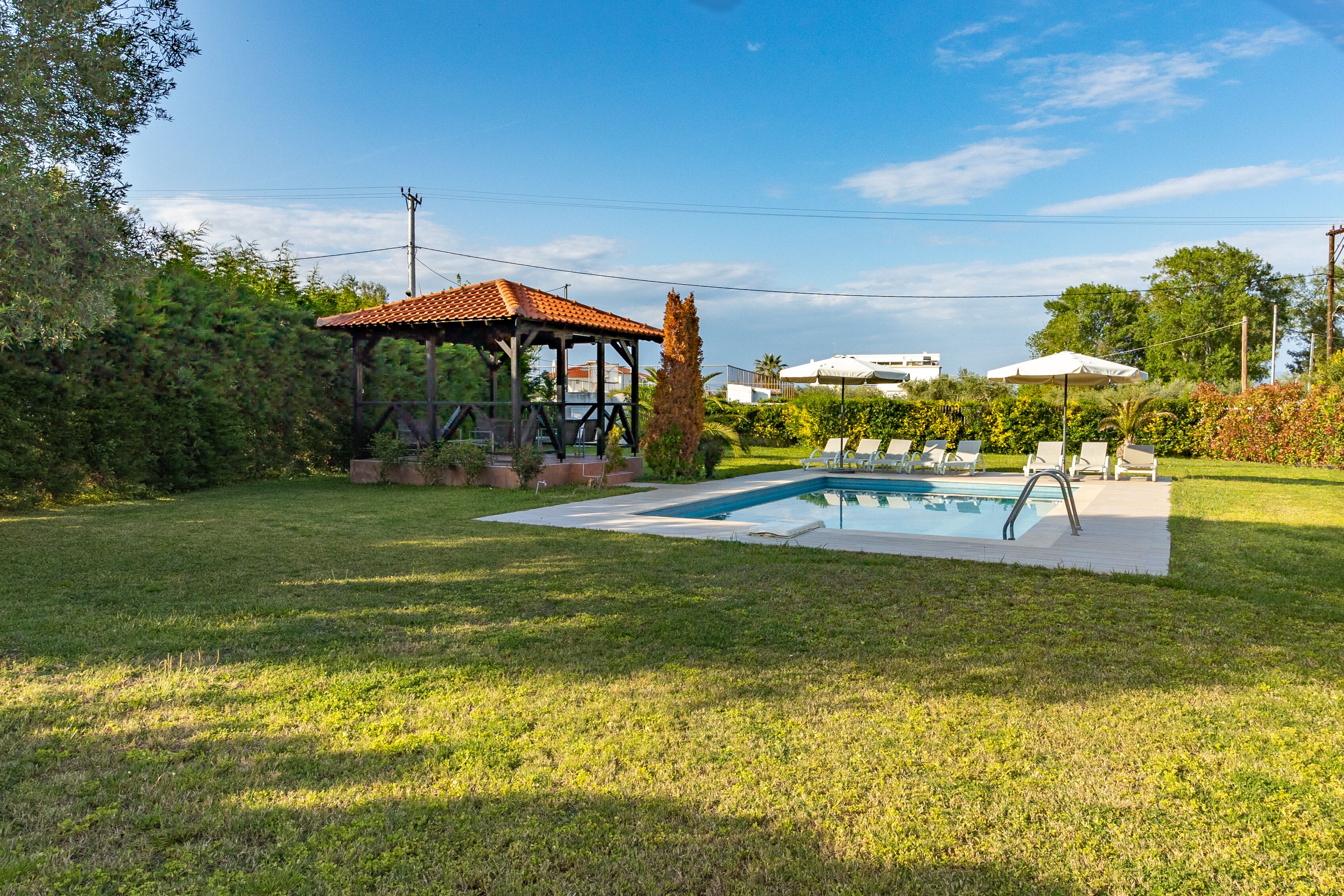 Um quintal com piscina, um gazebo e gramado.