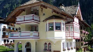 Um edifício de estilo chalé tradicional com varanda, janelas em arco e montanhas ao fundo.