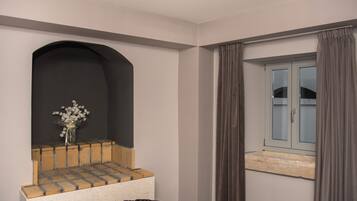 Quarto com banco embutido, pequena janela com cortinas e vaso com flores em um parapeito.