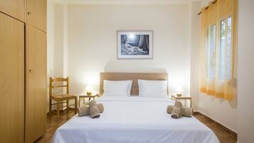 Quarto de hotel com uma cama grande, duas mesas de cabeceira com abajures, uma cadeira de madeira, um guarda-roupa e um quadro na parede.