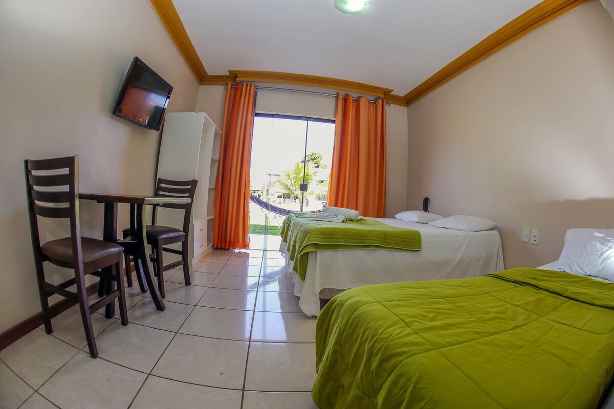 Quarto de hotel com duas camas, uma secretária com cadeiras, televisão e vista para o exterior.