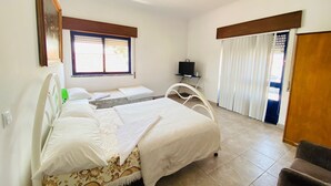 Quarto de hotel com uma cama, uma televisão sobre um suporte, uma janela com persianas e uma porta com cortinas.