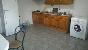 Cozinha compacta com armários de madeira, máquina de lavar embutida e geladeira.