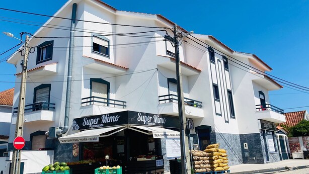 Um edifício de dois andares com fachada branca e uma placa que diz 'Super Mimo Supermercado'.