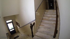 Uma escadaria com degraus de mármore e um corrimão, que leva a uma porta no topo.