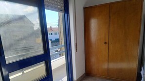 Quarto com um guarda-roupa de madeira grande, uma porta azul com painel de vidro e piso de azulejos.